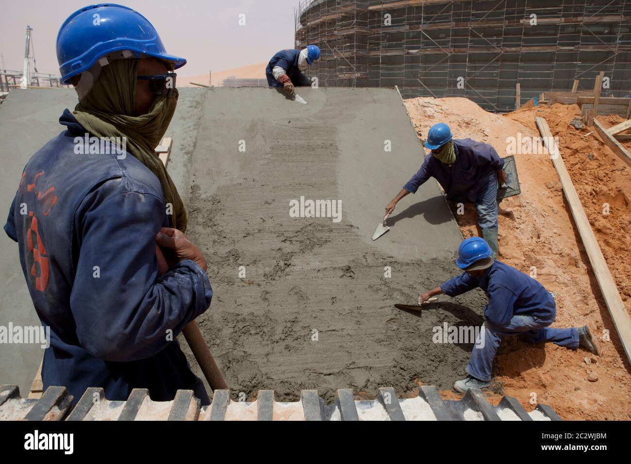 Consruction crew work on concrete sloping sides to an oil storage tank ...