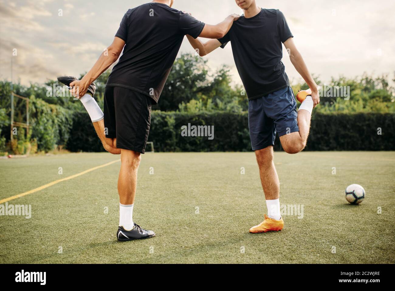 Two soccer players doing stretching exercise on the field. Football ...
