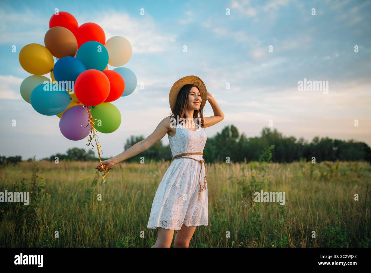 Smiling woman with colorful balloons walking in green field. Pretty ...