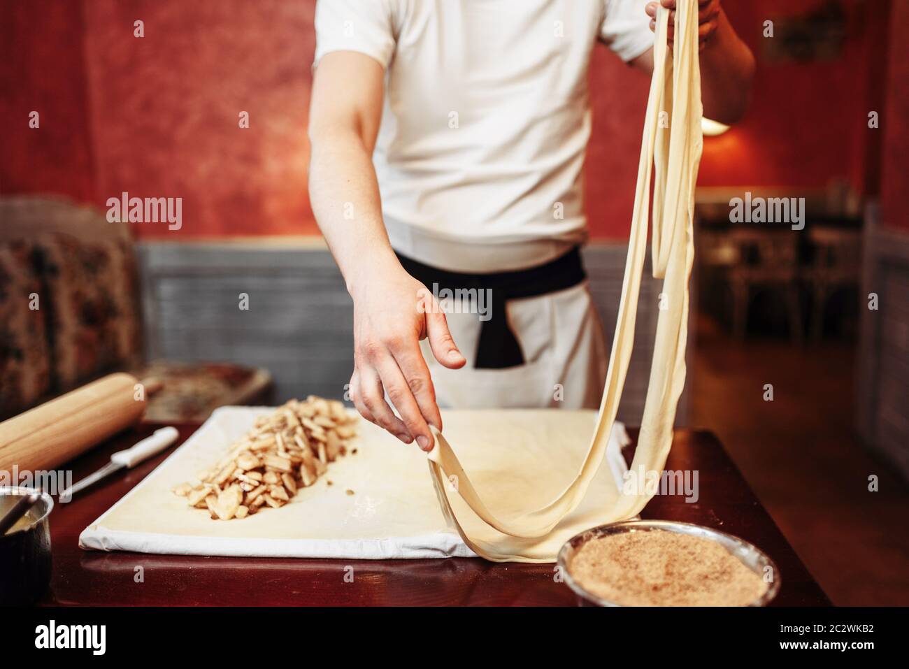 Male chef prepares dough for apple strudel on wooden kitchen table ...