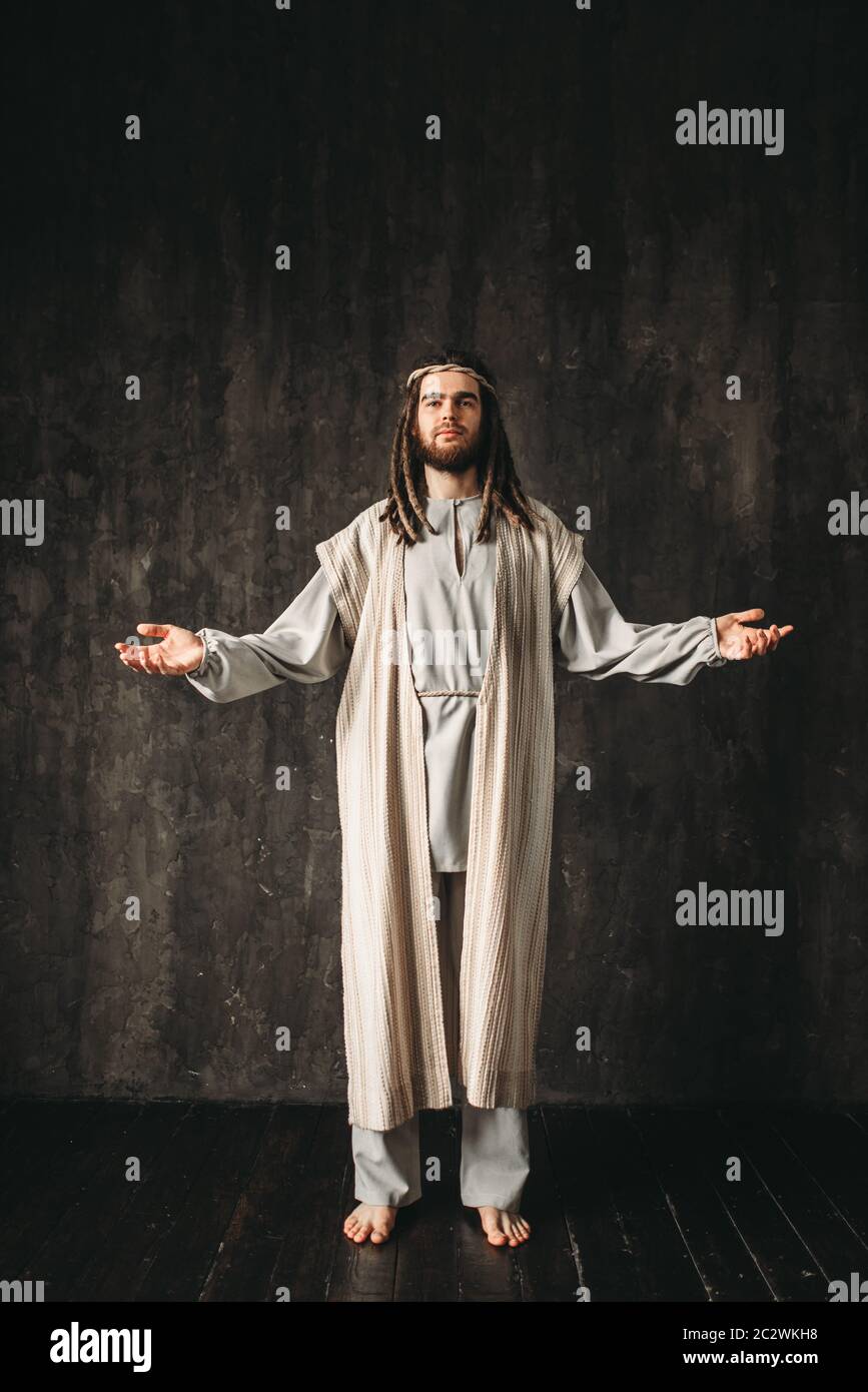 Jesus Christ in white robe praying with open arms, dark background. Son ...