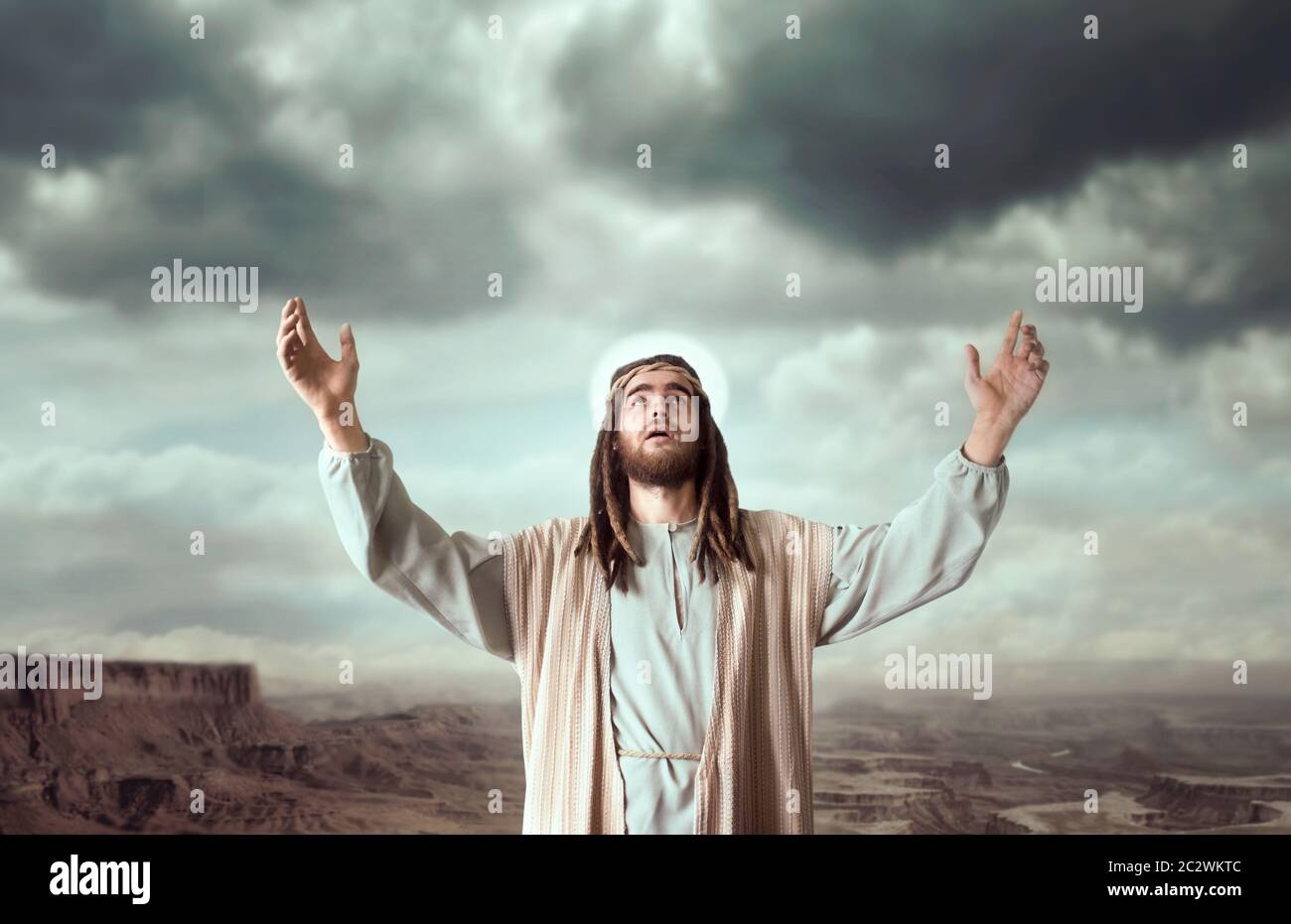 Jesus Christ in white robe praying with his hands up against cloudy sky ...