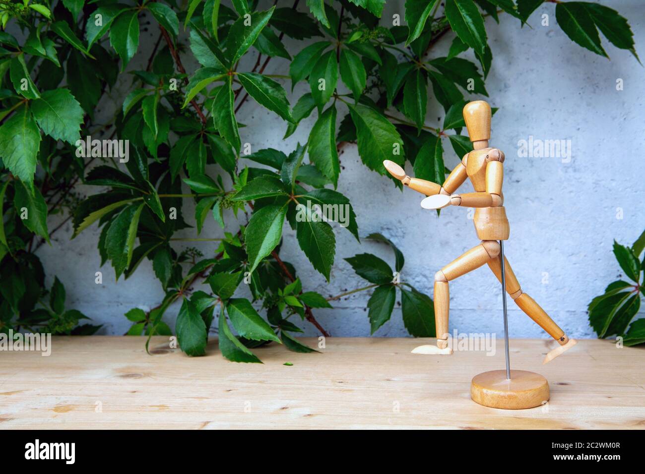 small wooden figure running in front of grey wall and plant Stock Photo ...