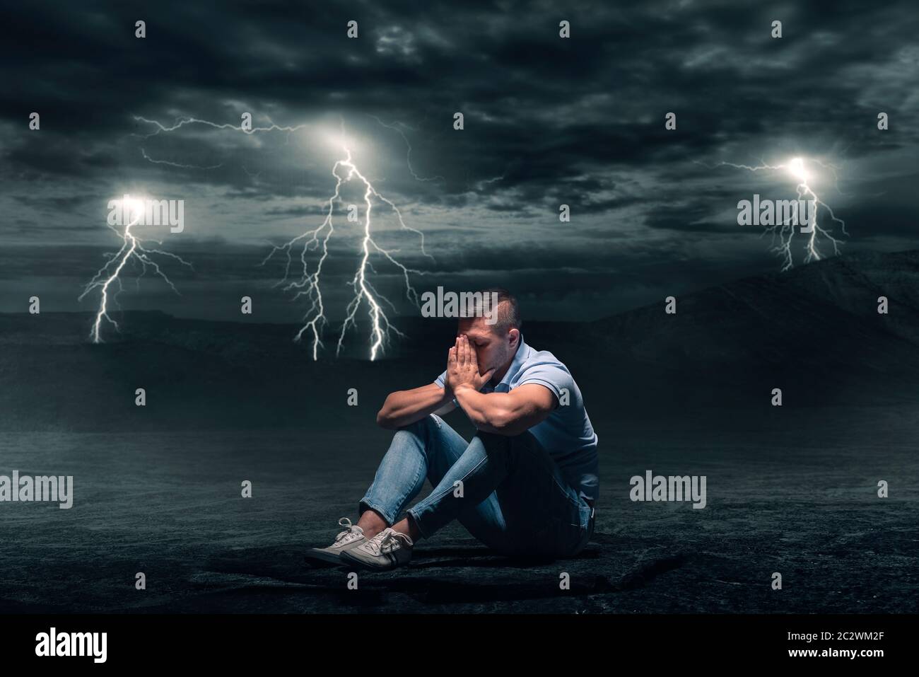 Young man sitting on the ground in desert, storm with lightning flash ...