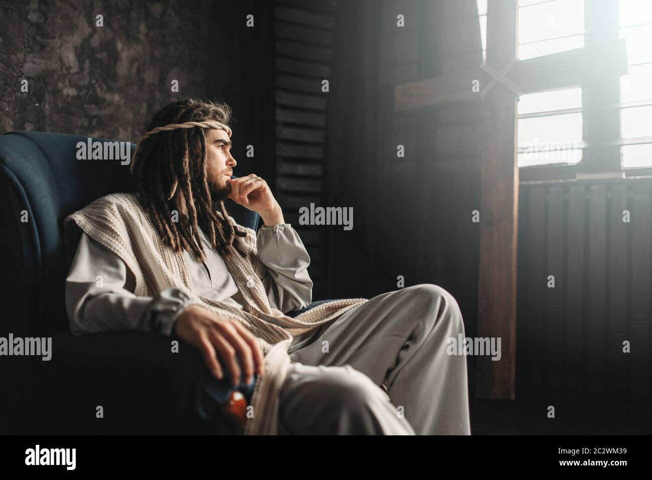 Thoughtful man in the image of Jesus Christ sitting in a chair against ...