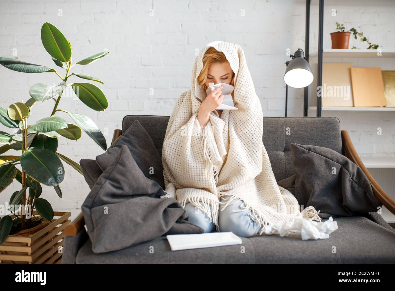 Young sick woman with kerchief sitting on couch under the blanket ...