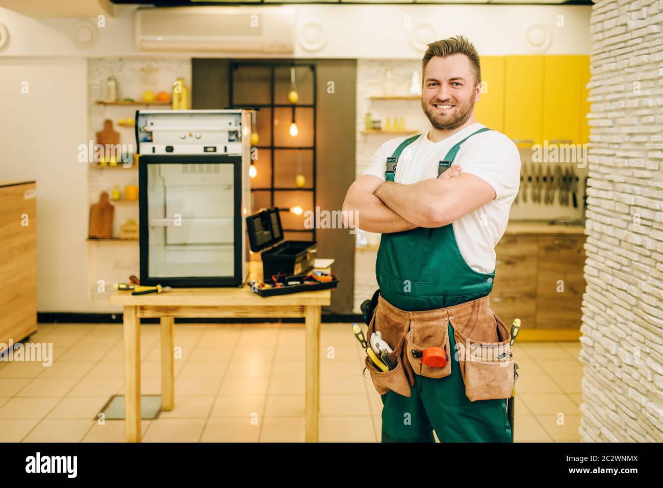 Worker in uniform against refrigerator on the table at home. Repairing ...