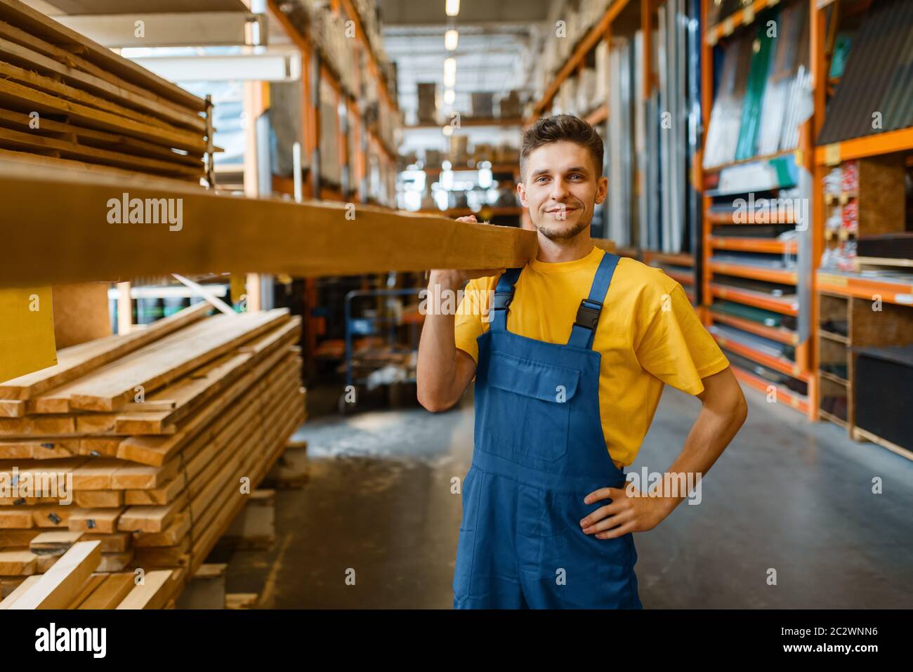 Male builder holds wooden boards in hardware store. Customer look at ...
