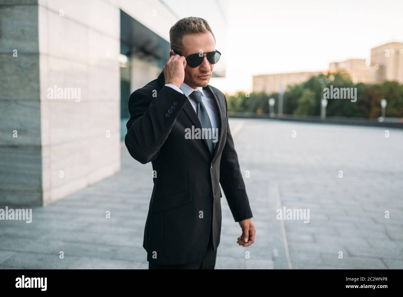 Male bodyguard in suit and sunglasses talking by security earpiece ...