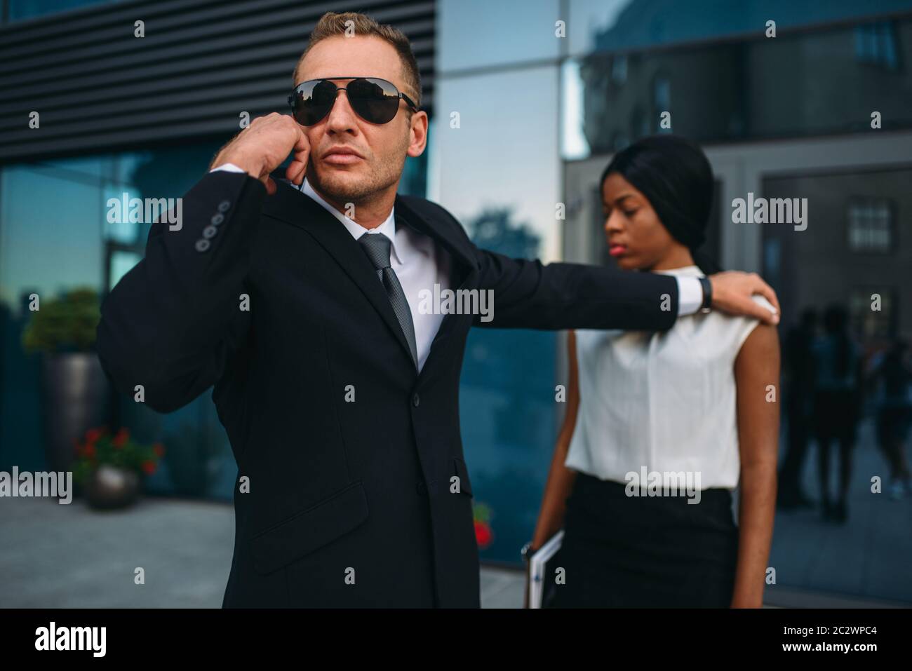 Serious bodyguard in suit and sunglasses requests support on earpiece ...