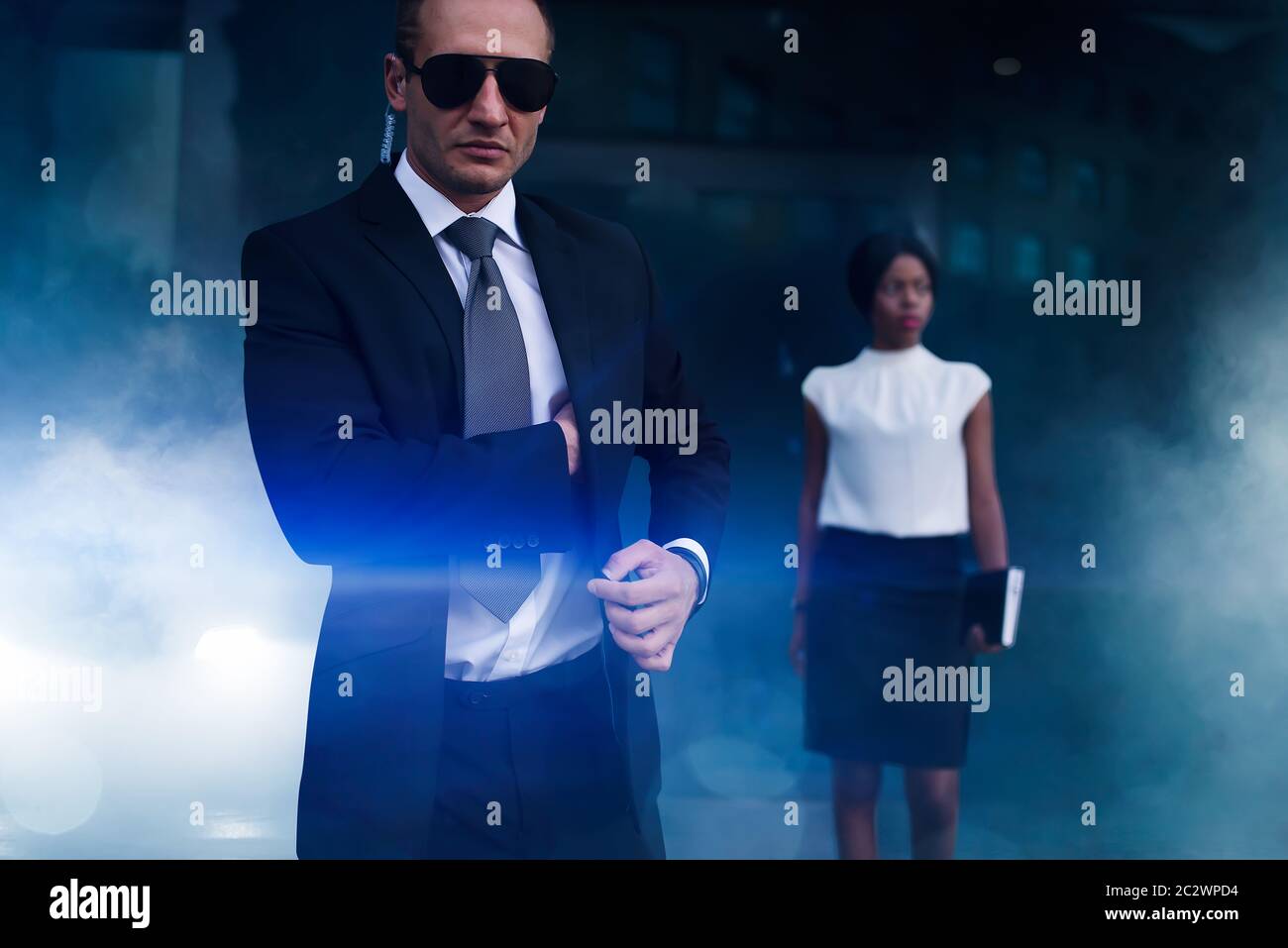 Serious bodyguard in suit, sunglasses and earpiece, female client on ...