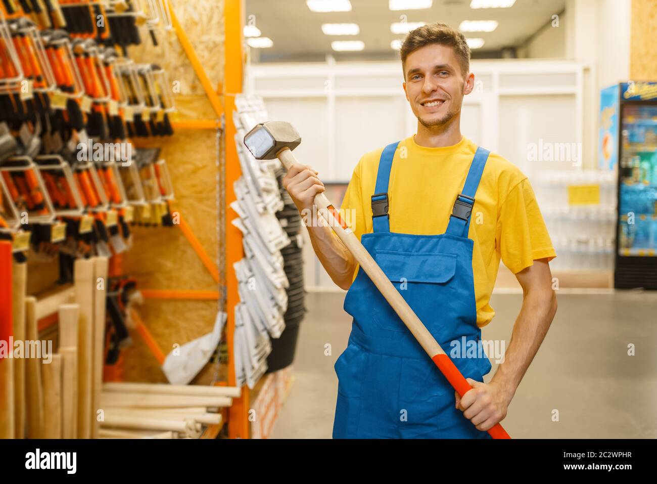 Male builder choosing sledgehammer at the shelf in hardware store ...