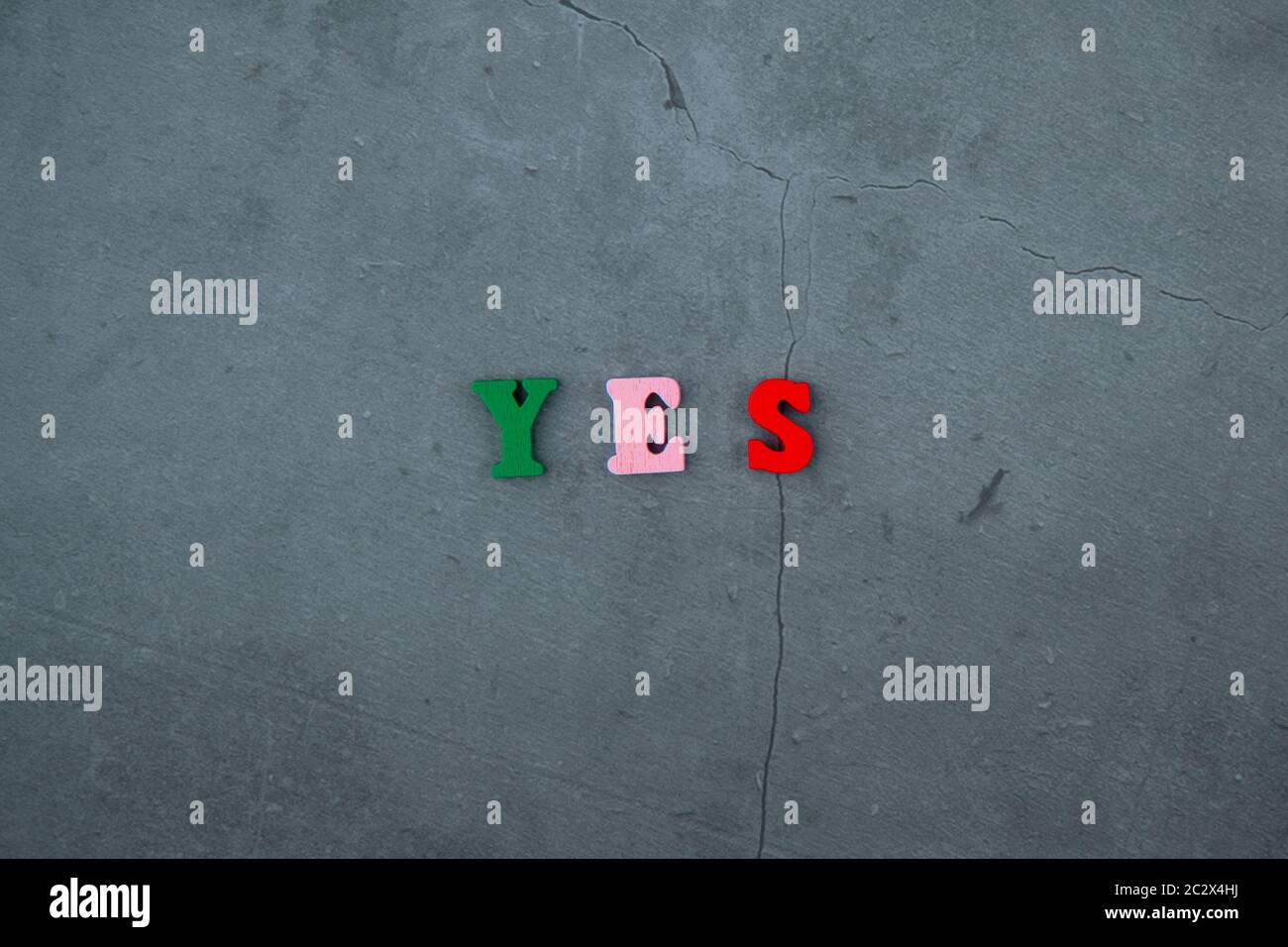 The multicolored Yes word is made of wooden letters on a grey plastered ...