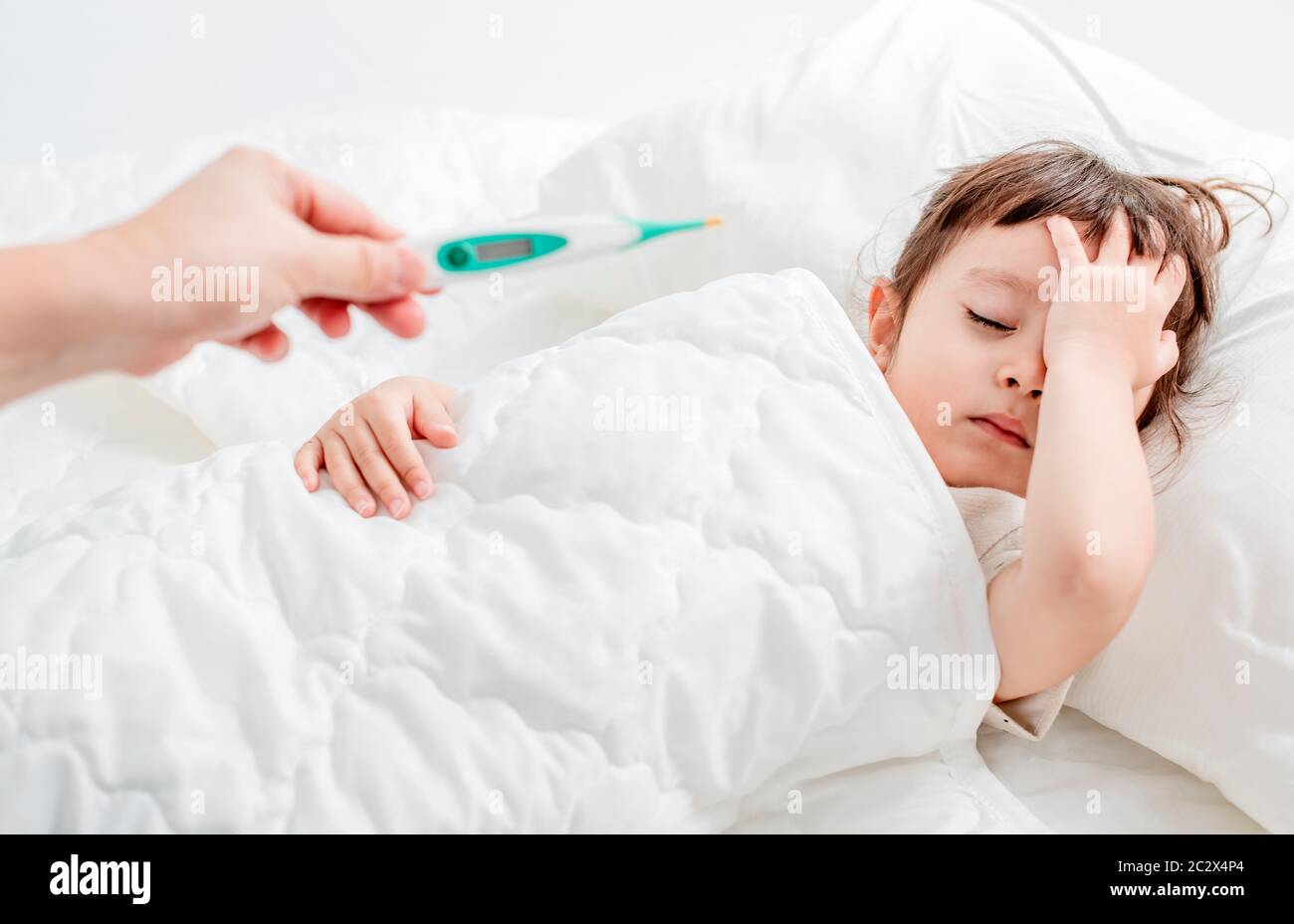 Sick child with flu fever laying in bed and mother holding thermometer ...