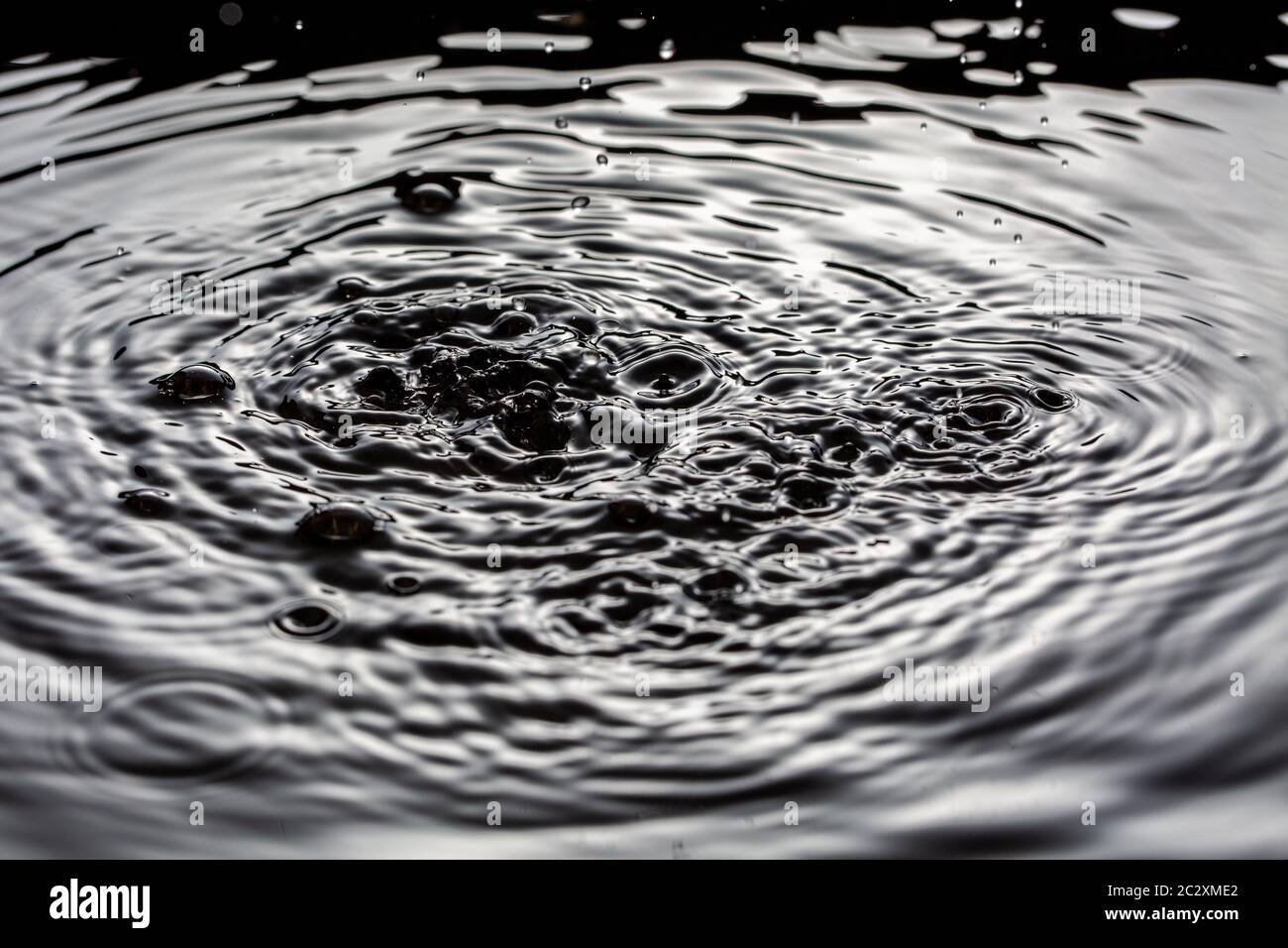 Drops of rain splashing into a puddle, water splashing making circular ...