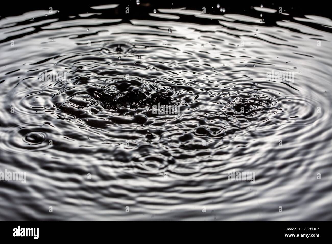 Drops of rain splashing into a puddle, water splashing making circular ...