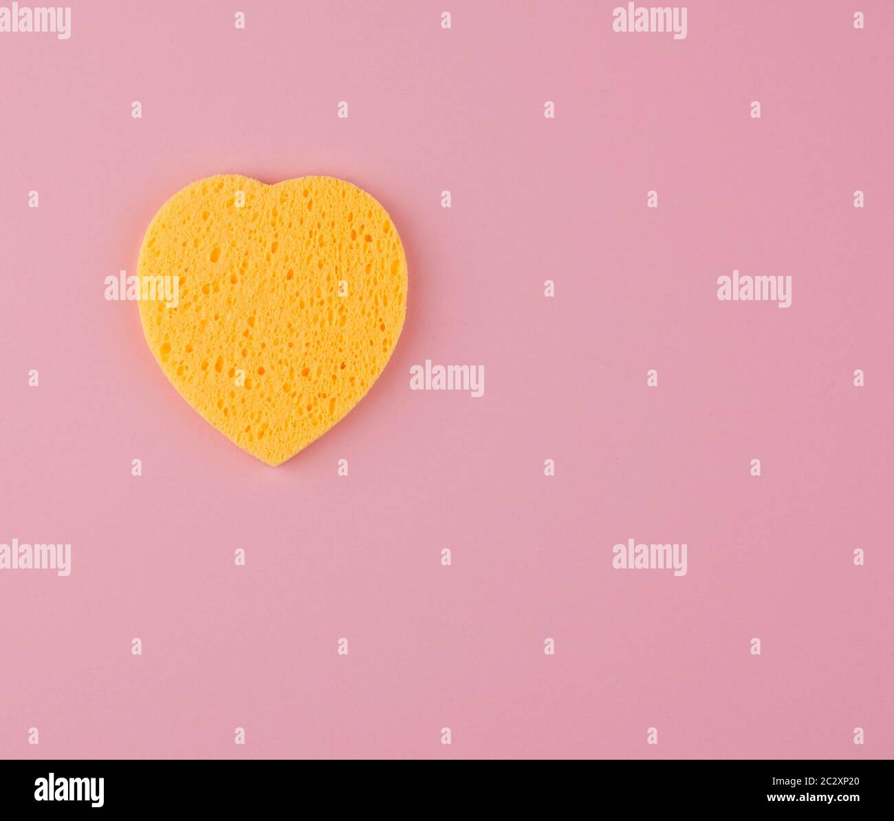 yellow heart shaped sponge for face wash on pink background, copy space ...
