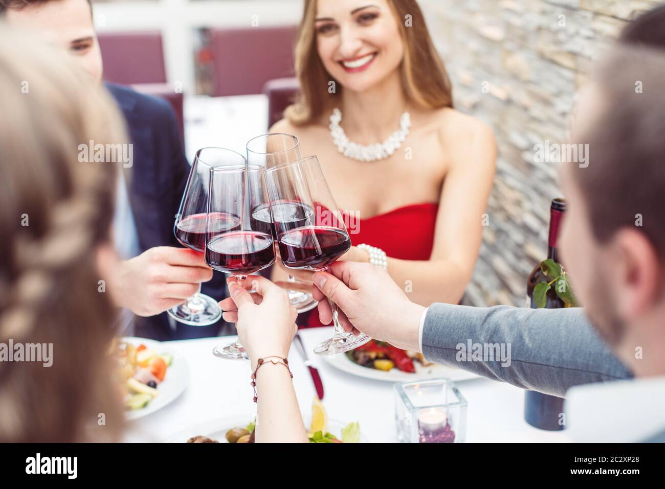 Group of cheerful people sitting on restaurant table toasting with red ...
