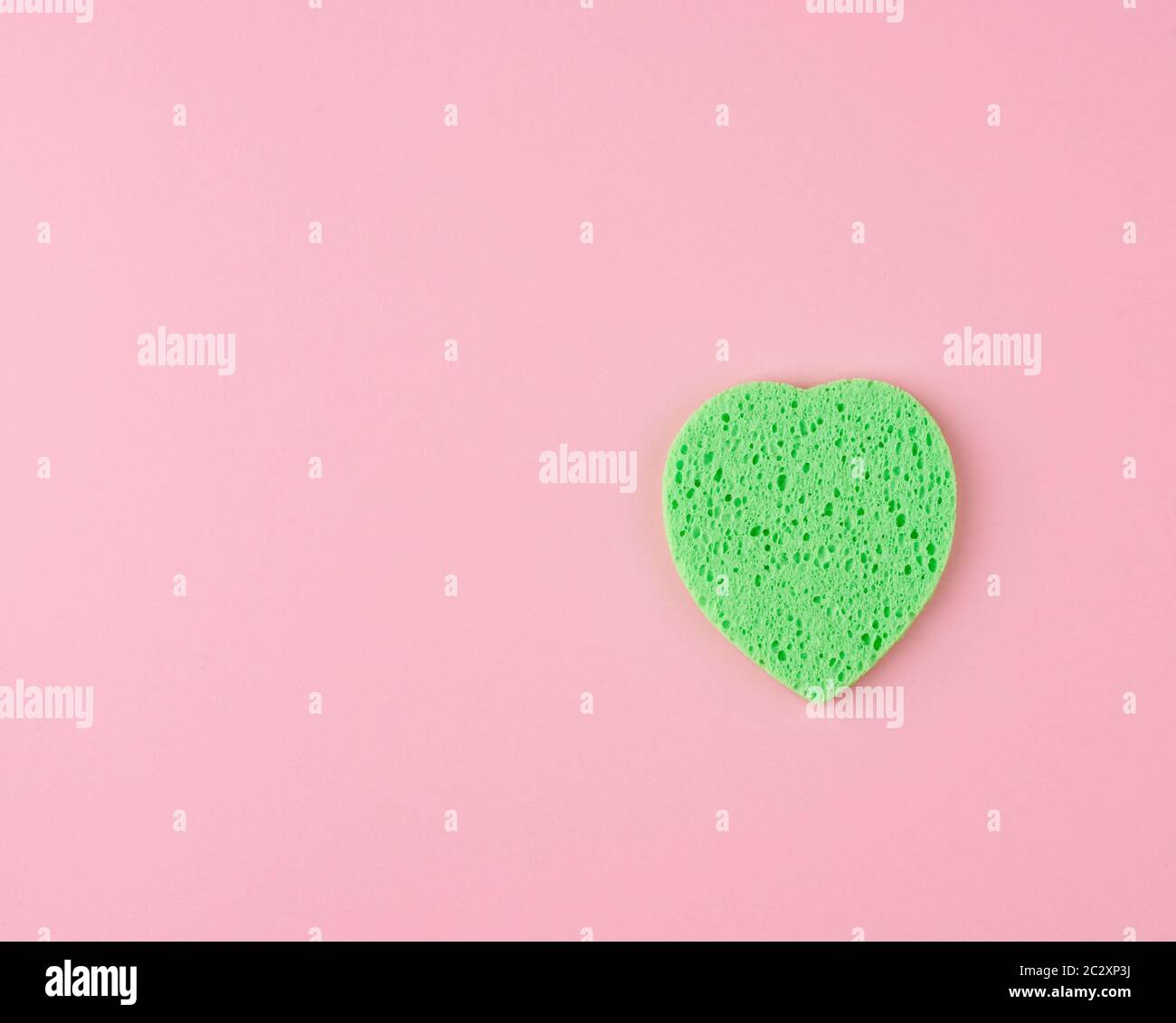 green heart shaped sponge for face wash on pink background, copy space ...