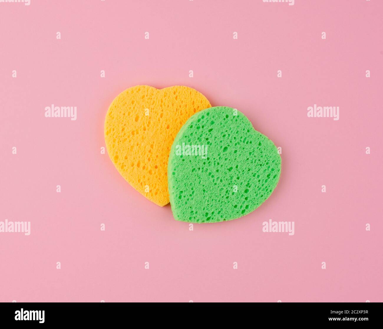 green and yellow heart shaped sponge for face wash on pink background ...