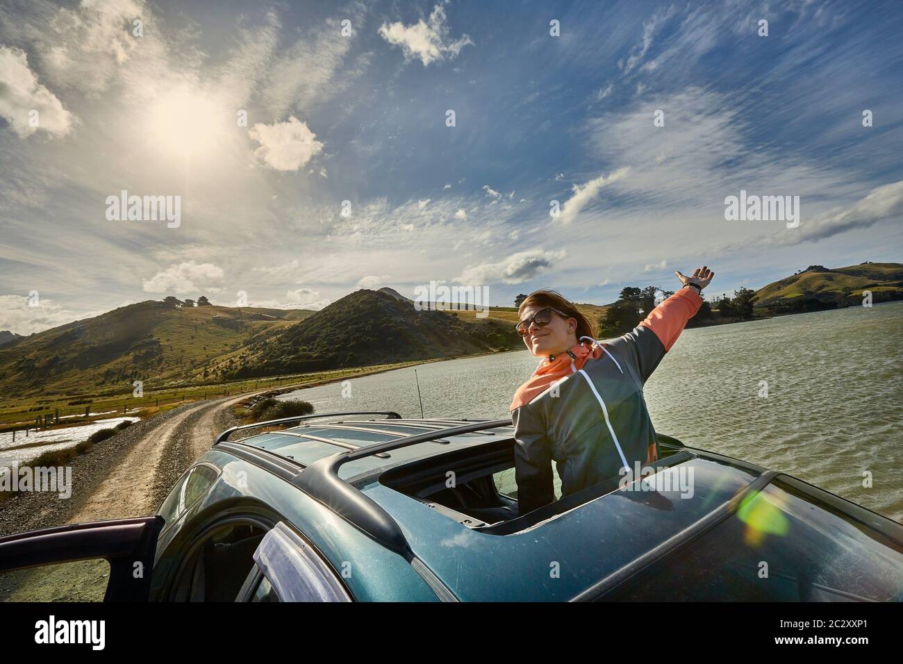 Woman leaning out through the sunroof of a car on a countryside journey ...