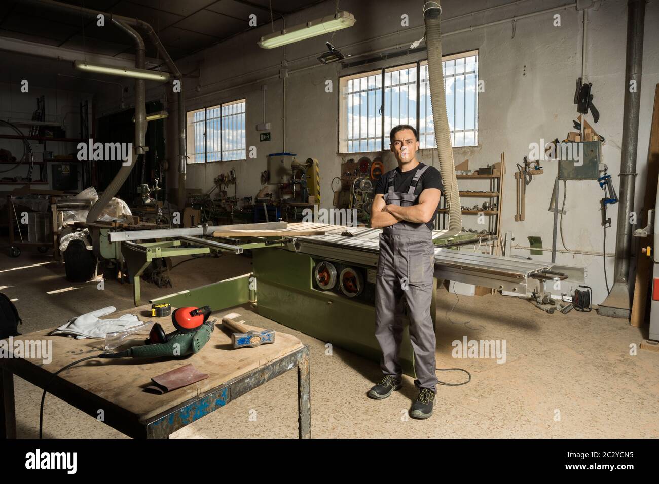 Worker standing looking at camera smiling in a factory. Long shot, full ...