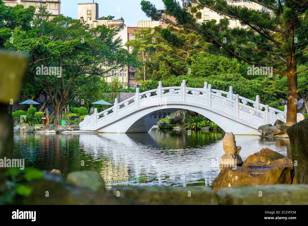 Chinese style white stone bridge over a small lake at a green park in ...