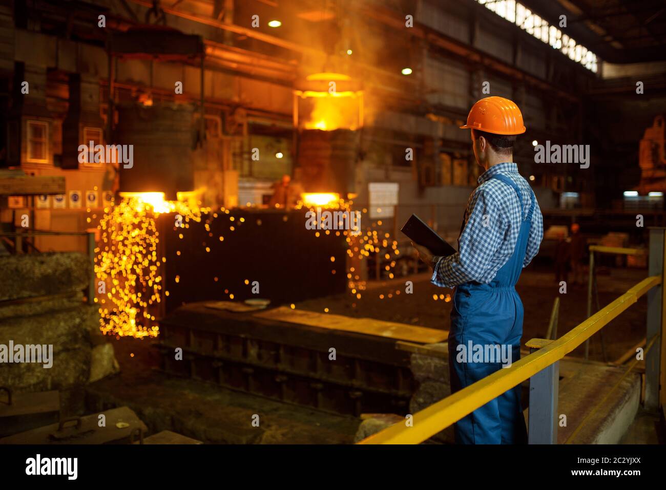 Master steelmaker in helmet at furnace with liquid metal, steel factory ...