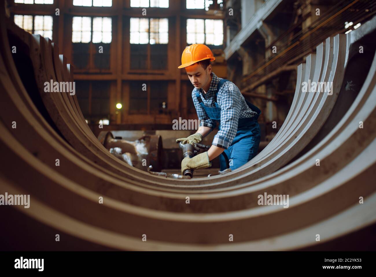 Male worker in uniform and helmet removes scale from metal workpieces ...