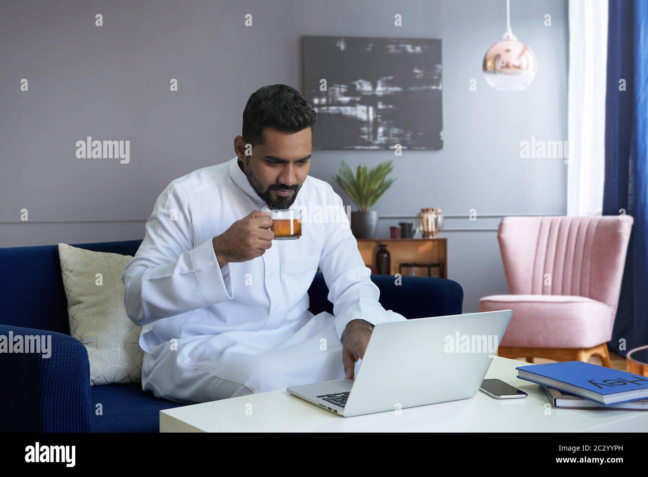 Saudi man drinking tea in living room at home using laptop Stock Photo ...