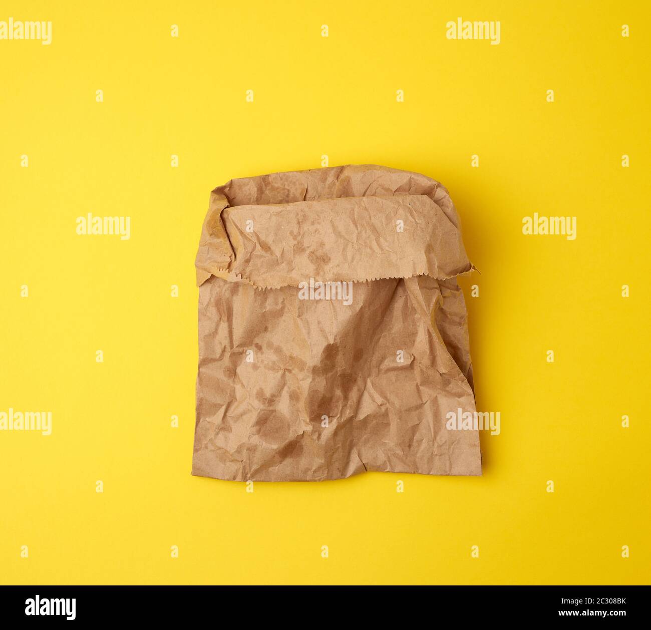 open brown paper bag for food packaging with greasy stains on a yellow ...