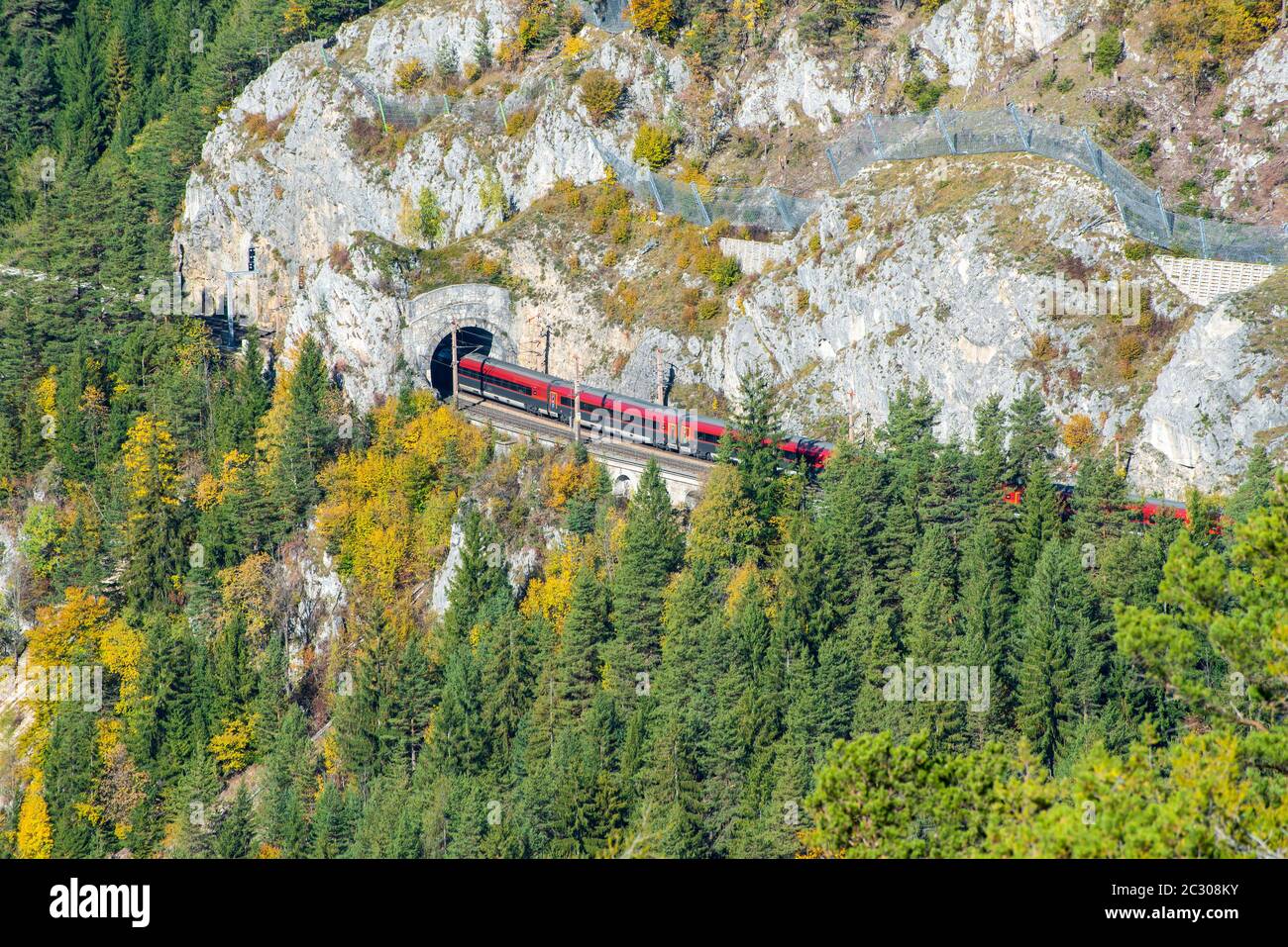 Red train on a viaduct between two tunnels on the Semmering Railway ...