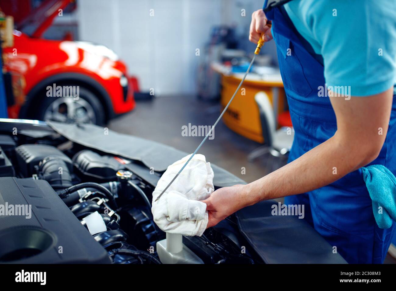 Worker in uniform checks the engine oil level, car service station ...