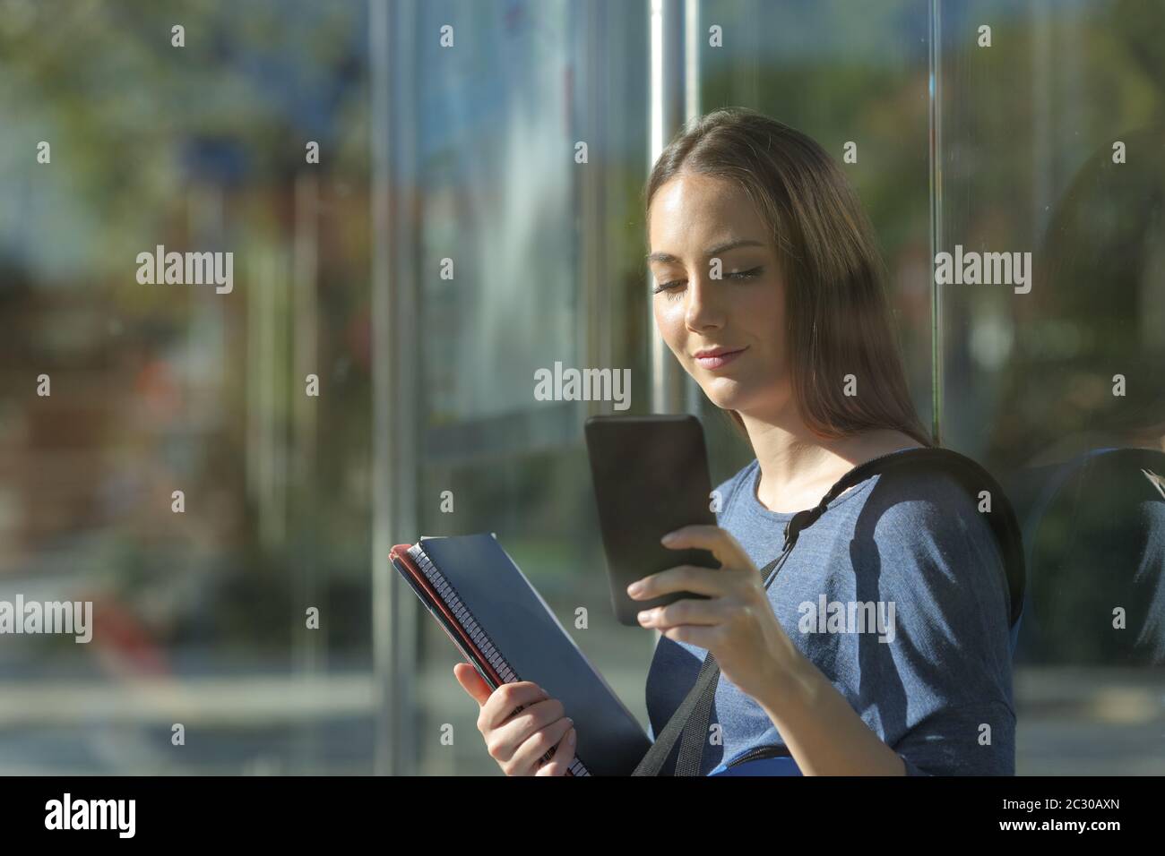 Student checking smart phone at the bus station monitoring transport ...