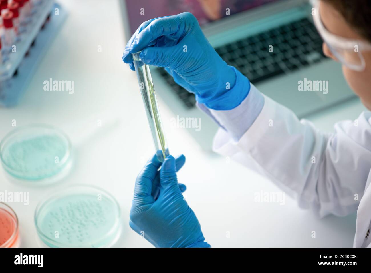 Close-up of biologist sitting at desk with petri dishes and mixing ...