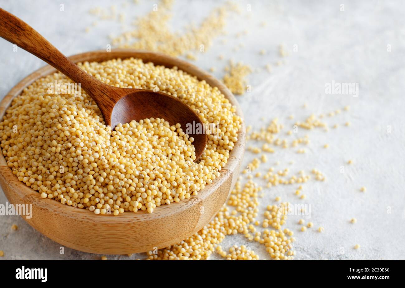 Raw dry hulled millet in a wooden bowl with a spoon with a copy space ...