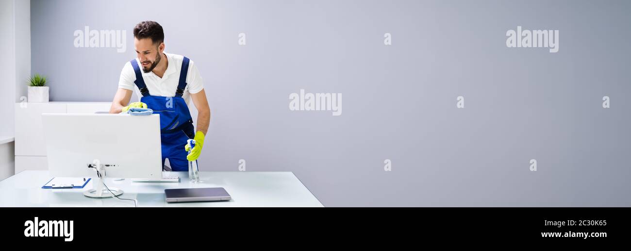 Portrait Of Happy Male Janitor Cleaning Computer On Office Desk Stock ...