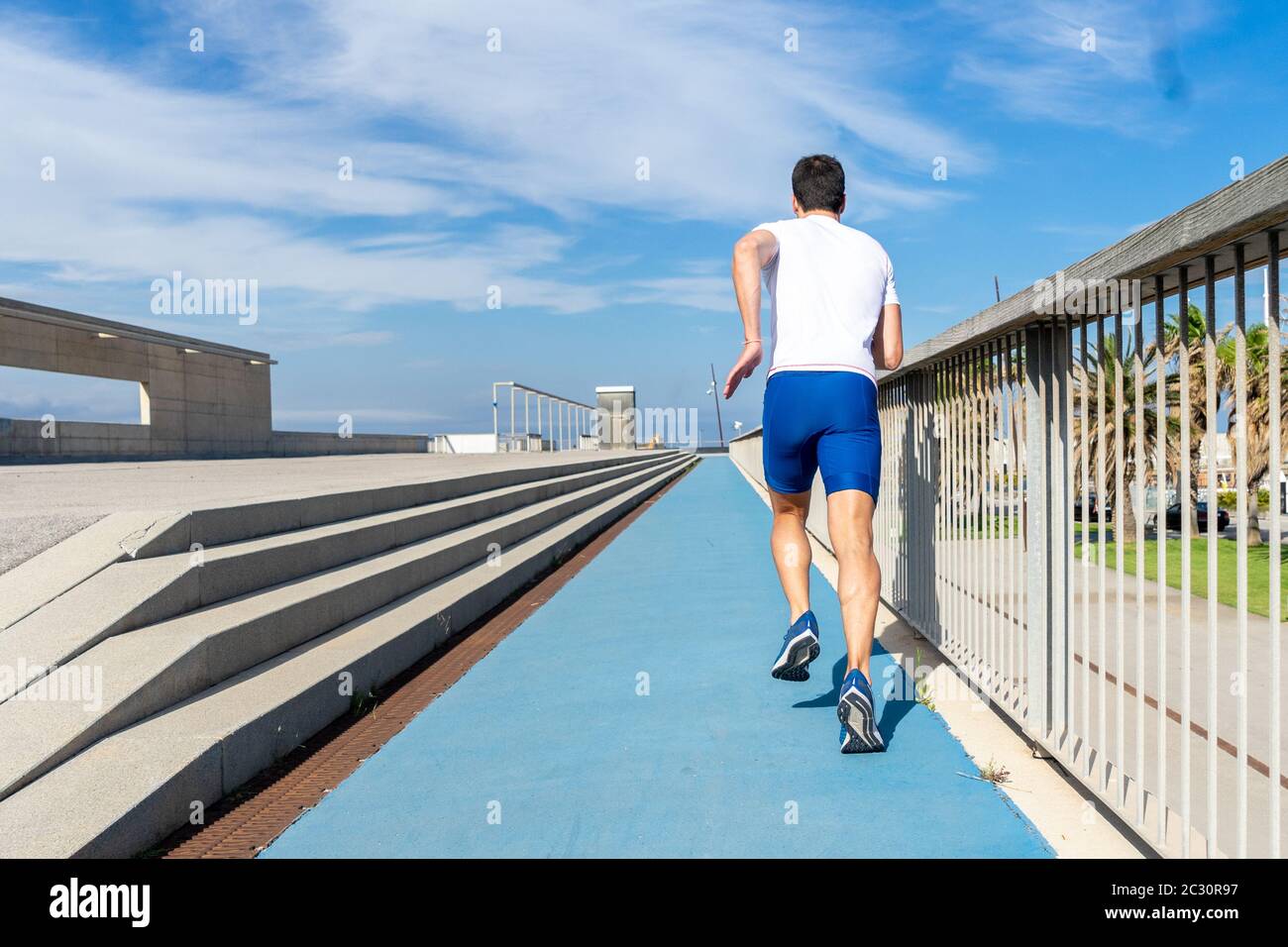 Young runner man in blue pants and white t-shirt running in the sun on ...