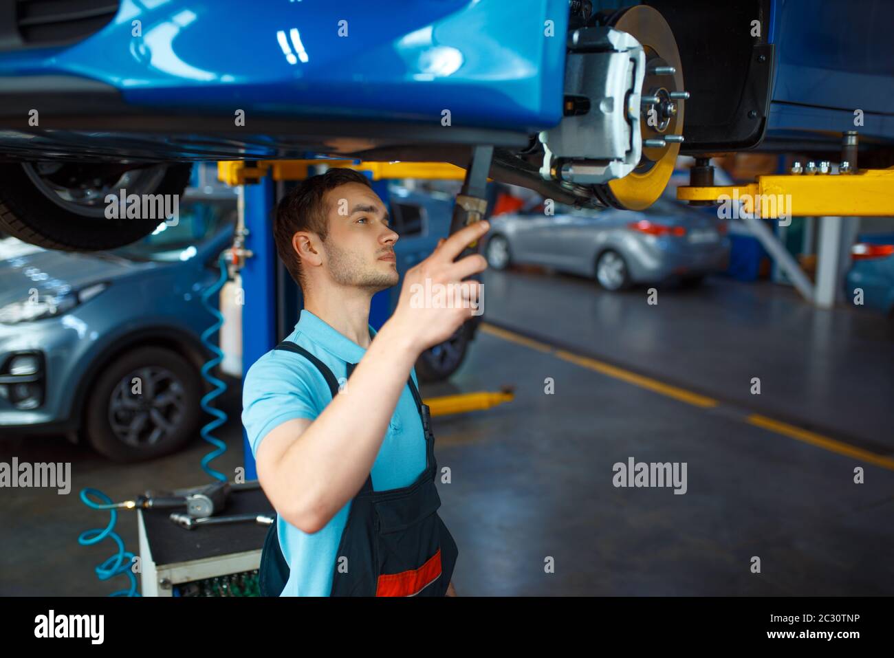 Worker in uniform checks vehicle suspension on lift, car service ...