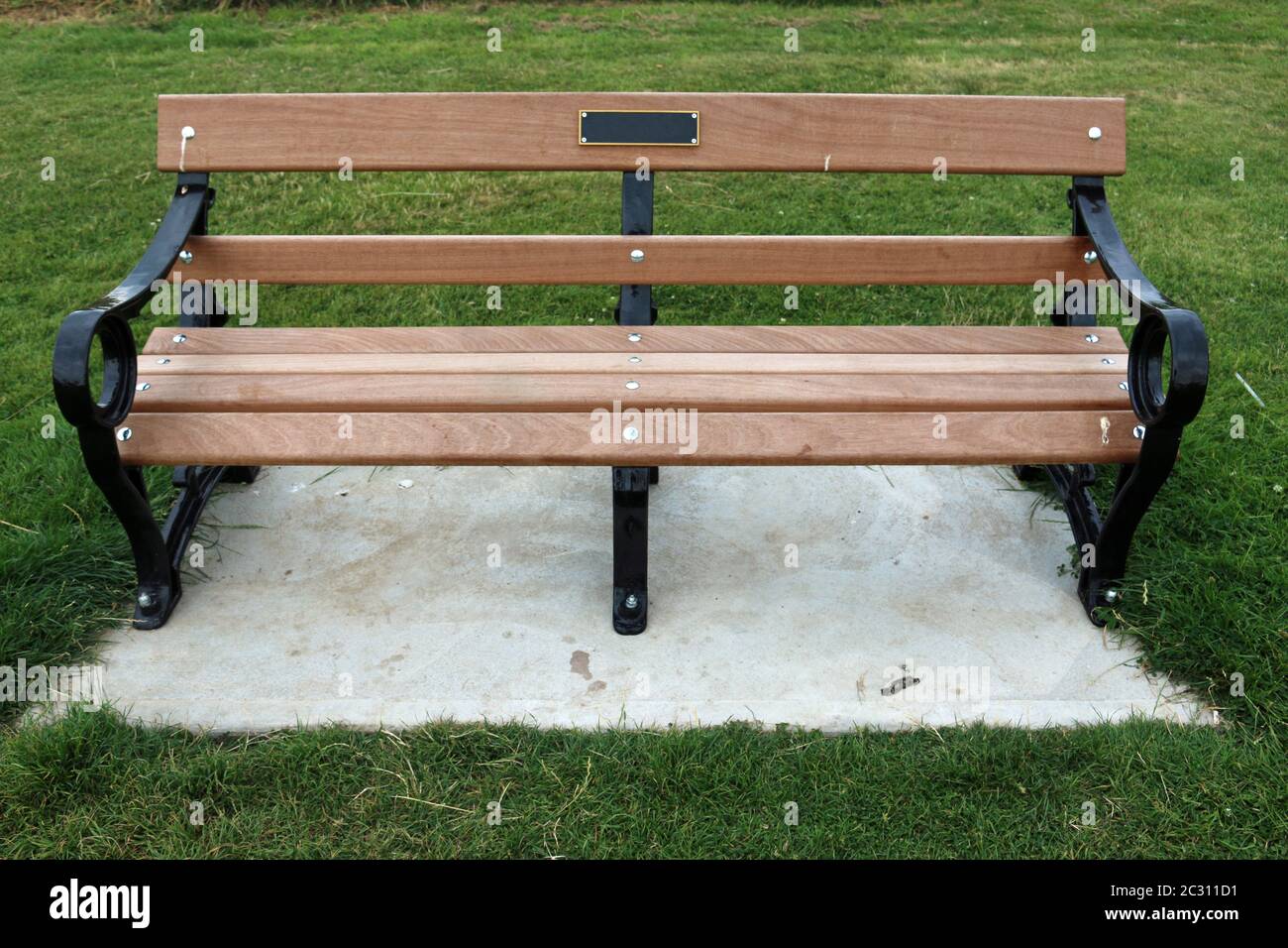 Metal framed wooden seat with a plaque standing on a concrete plinth ...