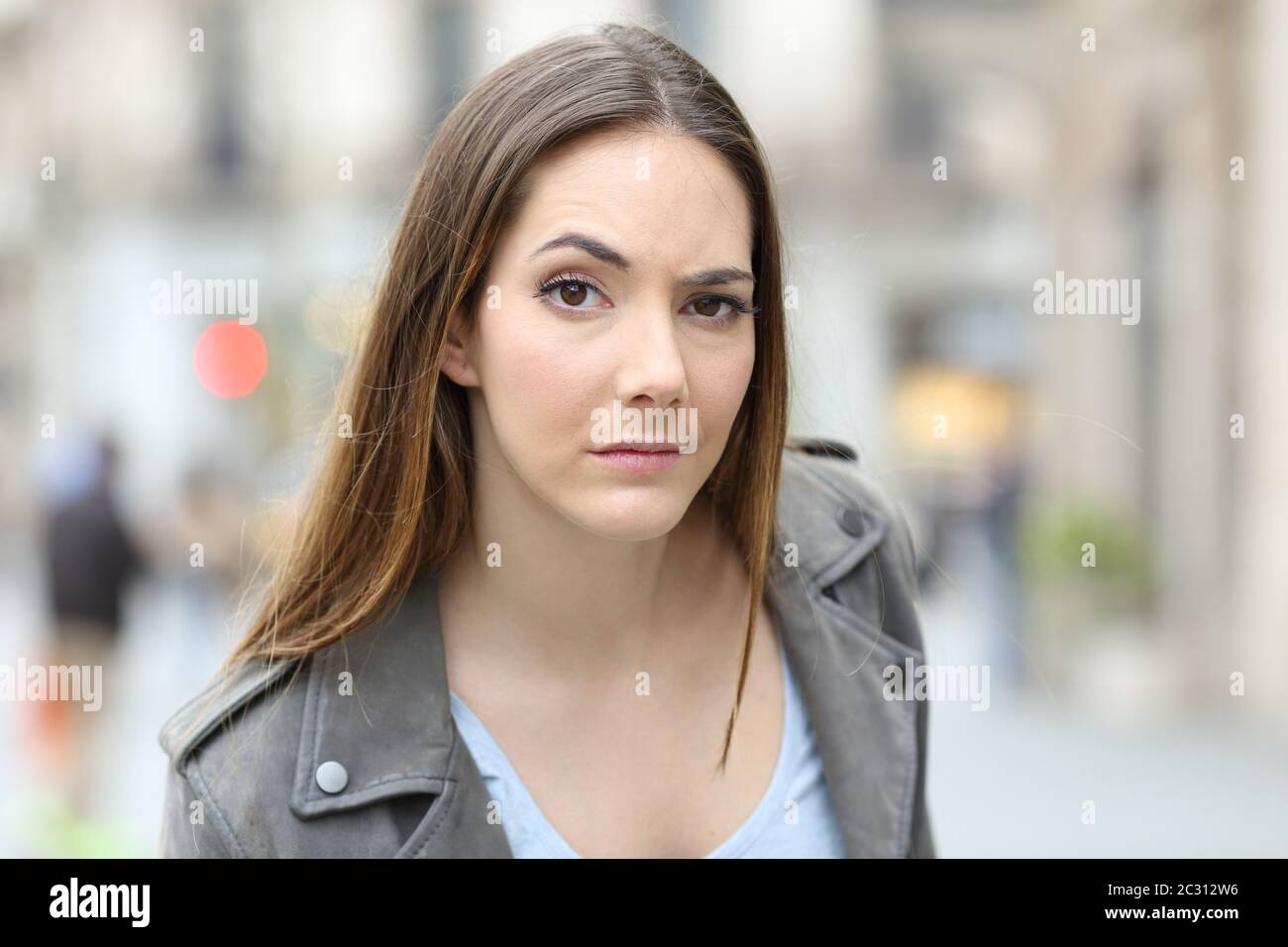 Portrait of a suspicious young woman looking at camera on city street ...