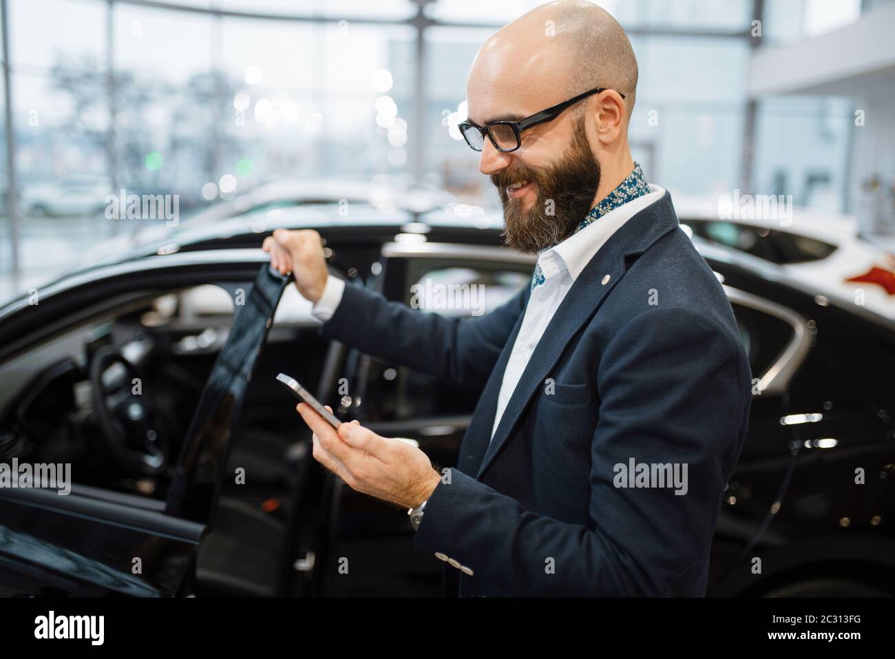 Man talks by mobile phone near new automobile in car dealership ...
