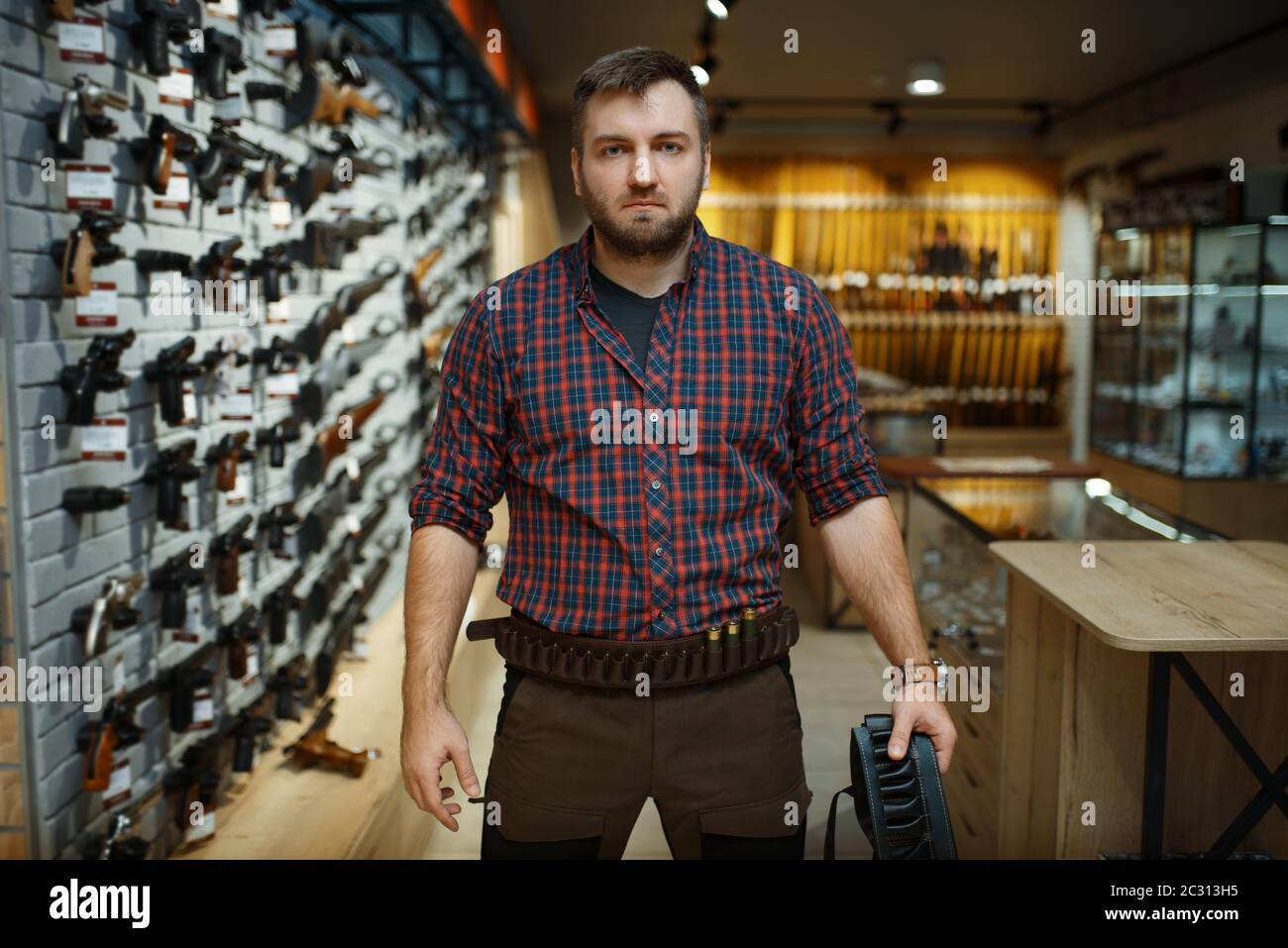 Man in hunting uniform holds ammo belt in gun shop. Euqipment for ...