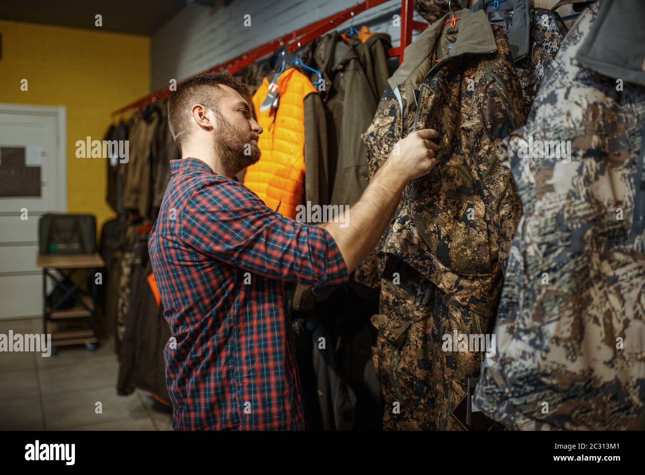 Man choosing uniform on showcase in gun shop. Euqipment and rifles for ...