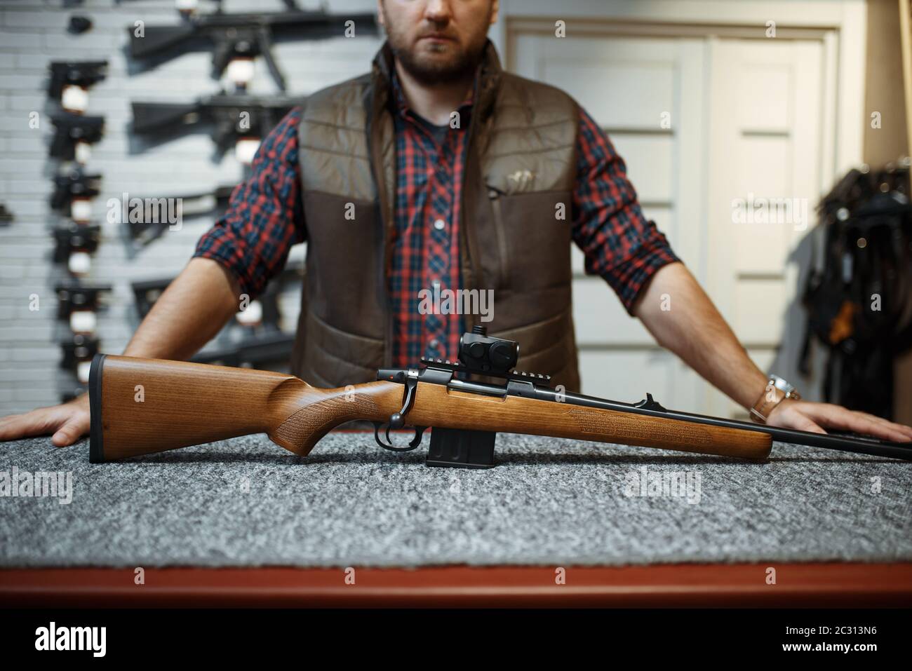 Man with rifle standing at counter in gun shop. Euqipment for hunters ...