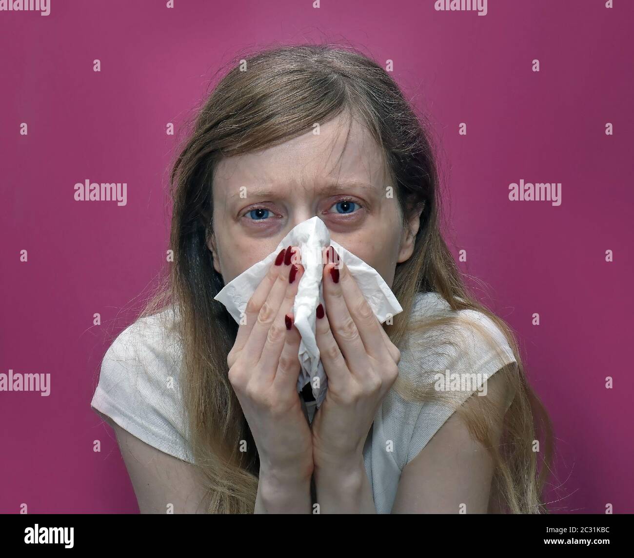 Sick young woman blowing her nose into paper tissue Stock Photo - Alamy