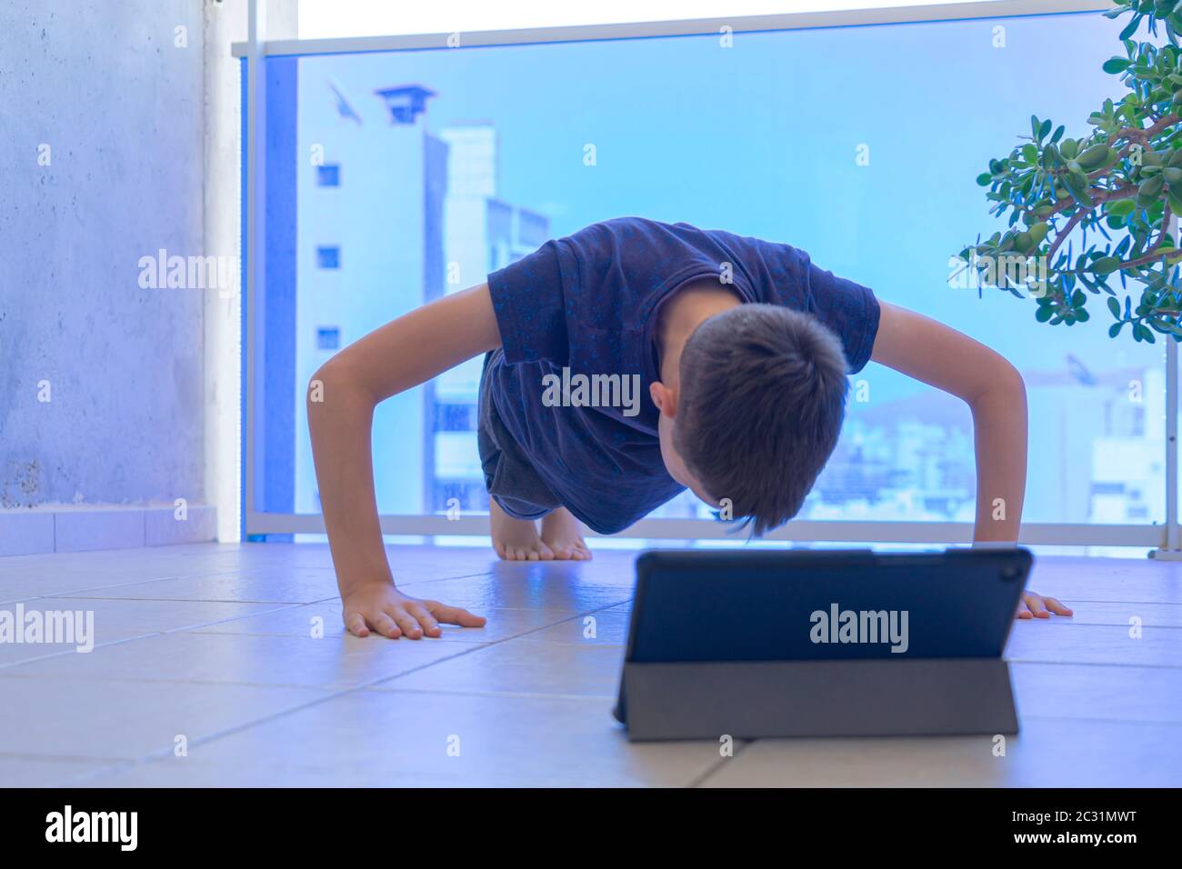 Kid with tablet computer doing push-ups sport exercises on balcony ...