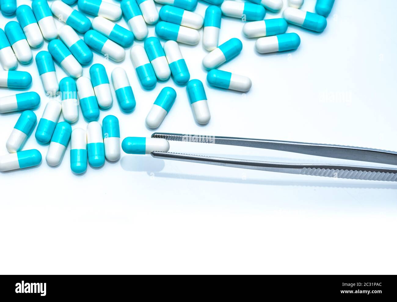 Forceps pick white-blue capsule from group of capsule pills. Drugs ...
