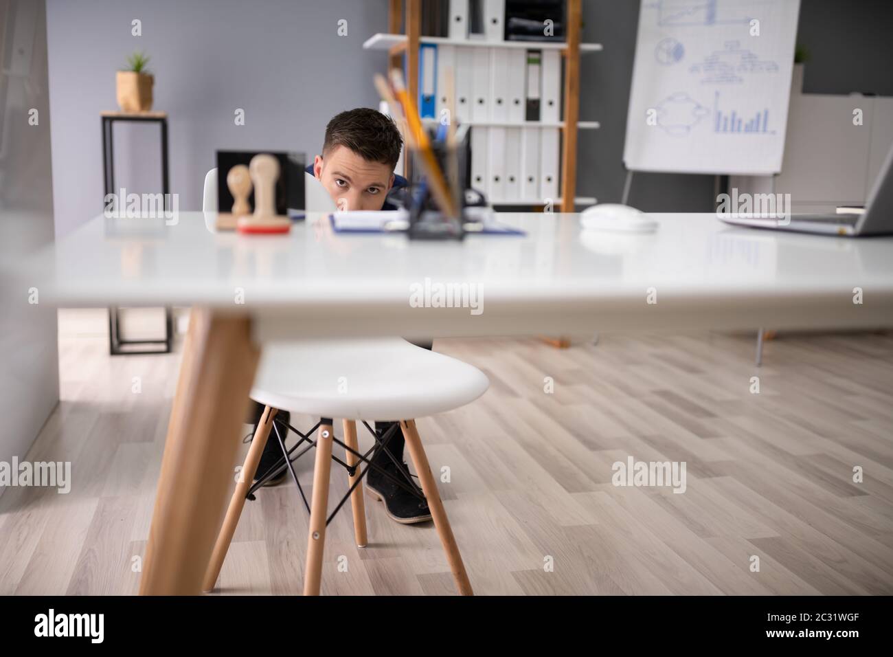 Frightened Young Businessman Hiding Behind Chair At Workplace Stock ...