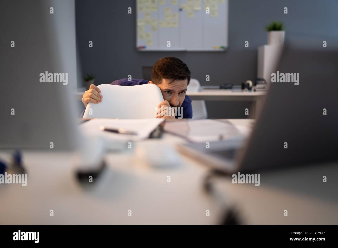 Frightened Businessman Hiding Behind Chair At Workplace Stock Photo - Alamy